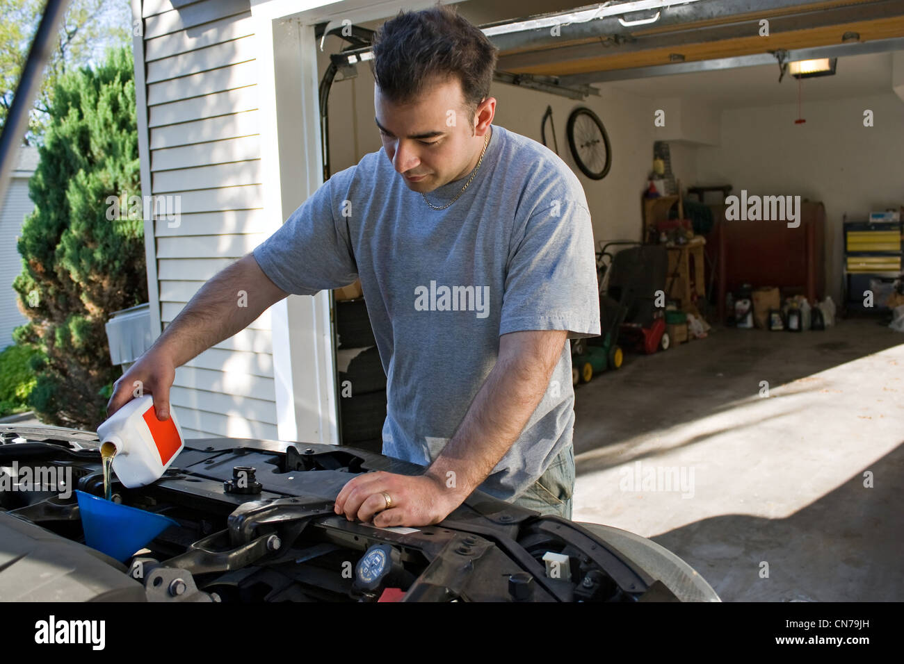 A young man adding oil to his cars engine at the end of an oil change ...