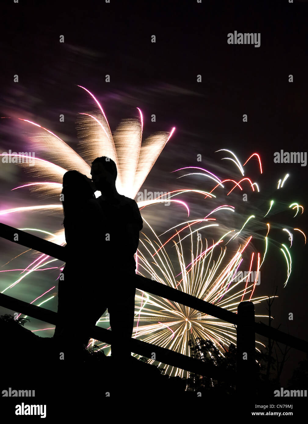 A silhouette of a kissing couple in front of a huge fireworks display ...