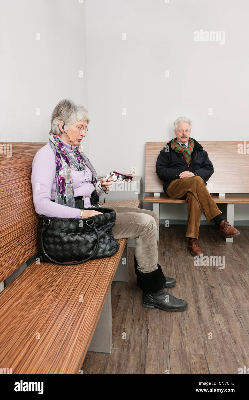 Elderly woman sitting in a waiting room, listening to music on her ...
