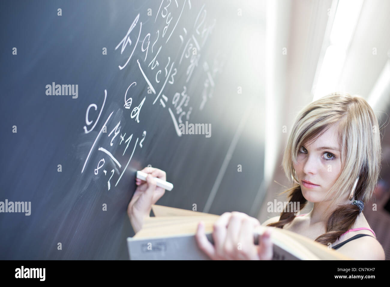 pretty young college student writing on the chalkboard/blackboard ...