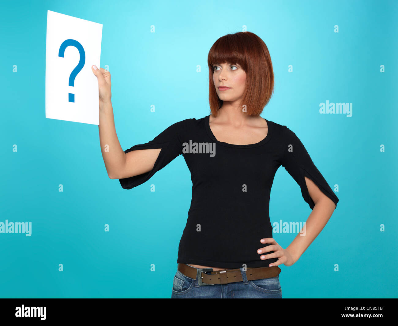 beautiful, young woman looking at a question mark on a white piece of ...