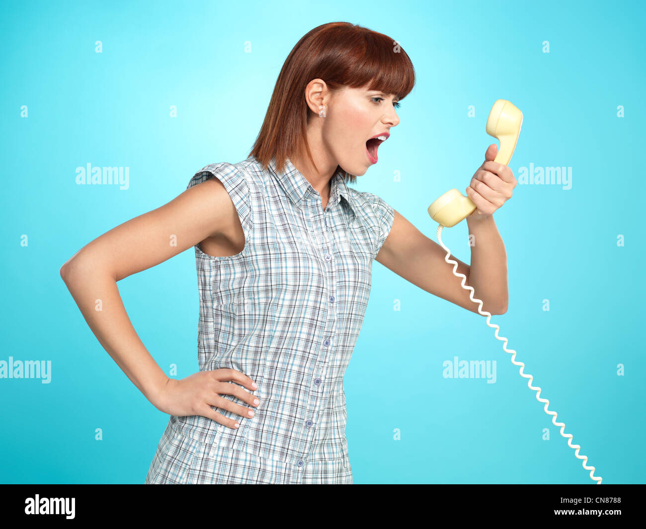 beautiful young woman, screaming on the telephone, on blue background ...