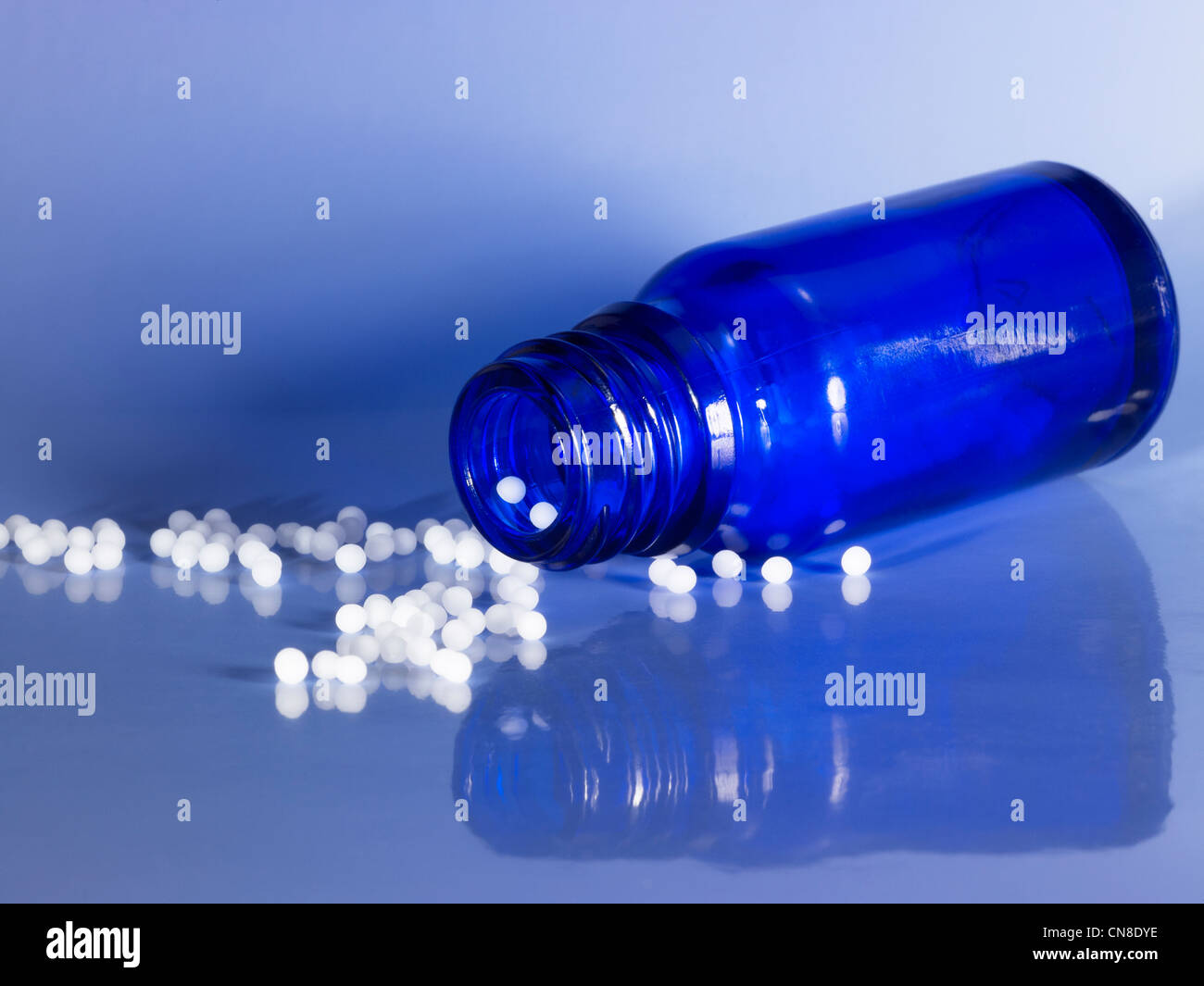 a open small blue bottle on reflective ground with globules around ...