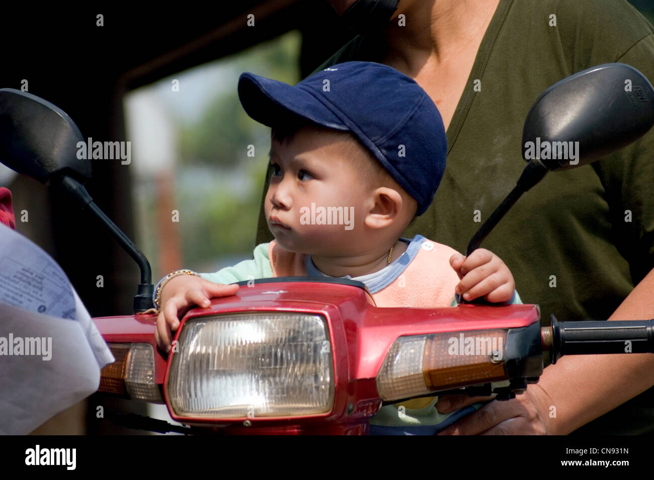 A two year old Asian boy is riding on a motorcycle with a man on a city ...