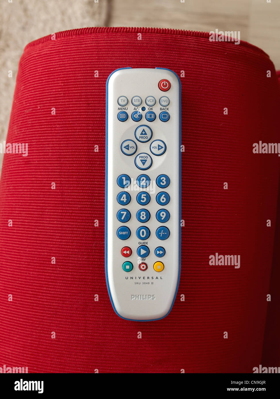 Television Remote control on arm of red sofa Stock Photo - Alamy