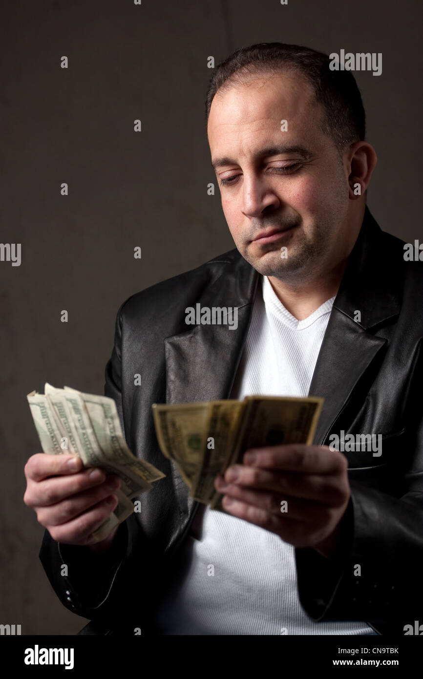 A shady looking man counting a handful of one hundred dollar bills ...
