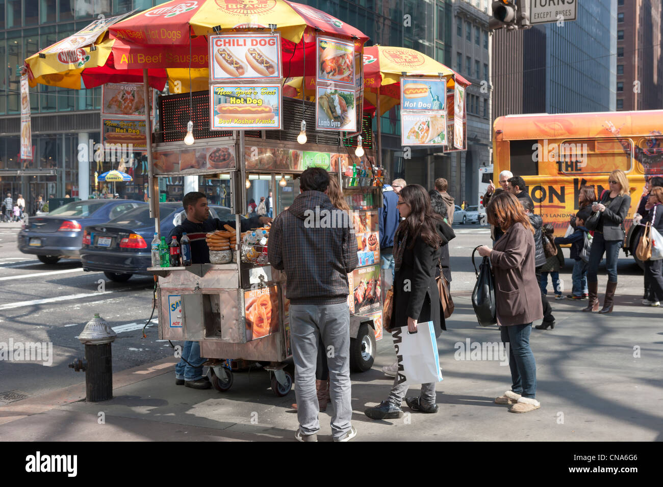 A street vendor cart selling hot dogs and other food works the corner ...