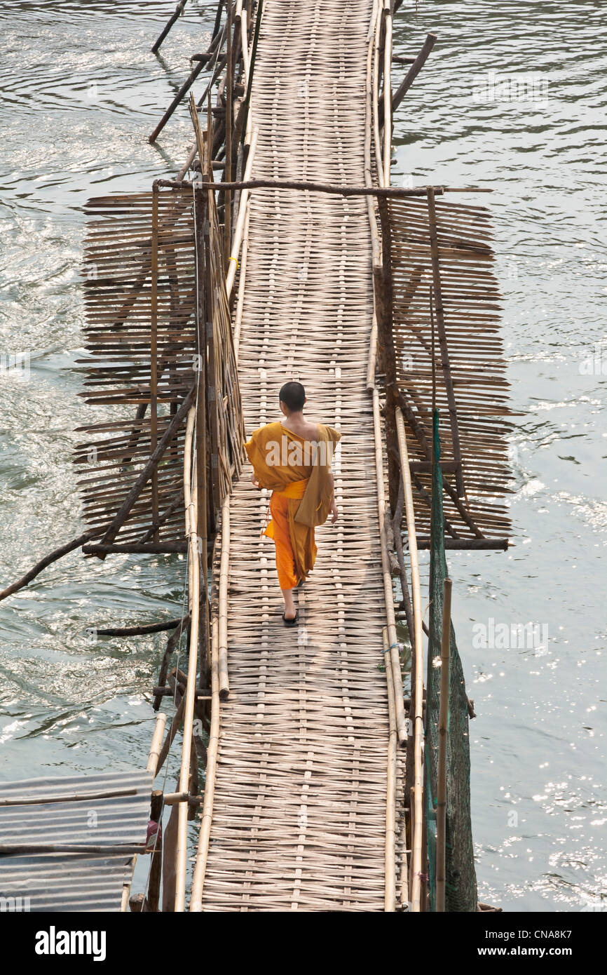 A young Buddhist monk walking across a bamboo bridge in Luang Prabang ...