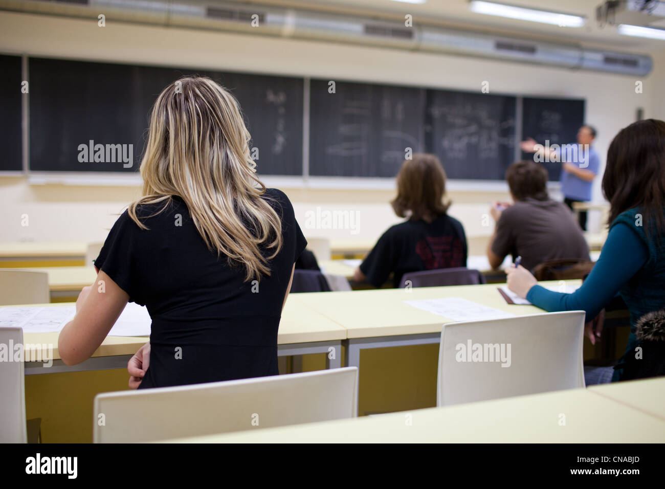 young pretty female college student sitting in a classroom full of ...