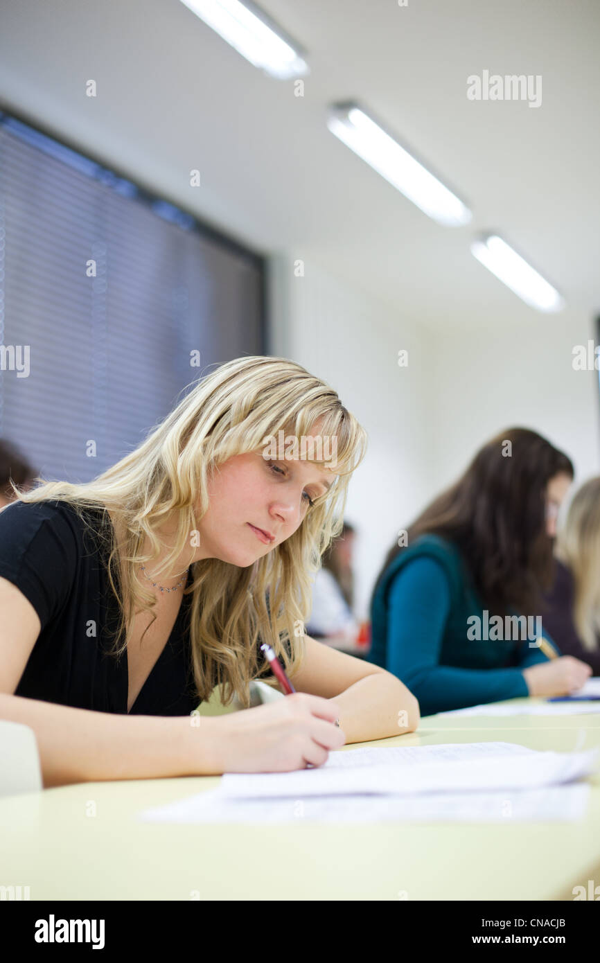 young pretty female college student sitting in a classroom full of ...