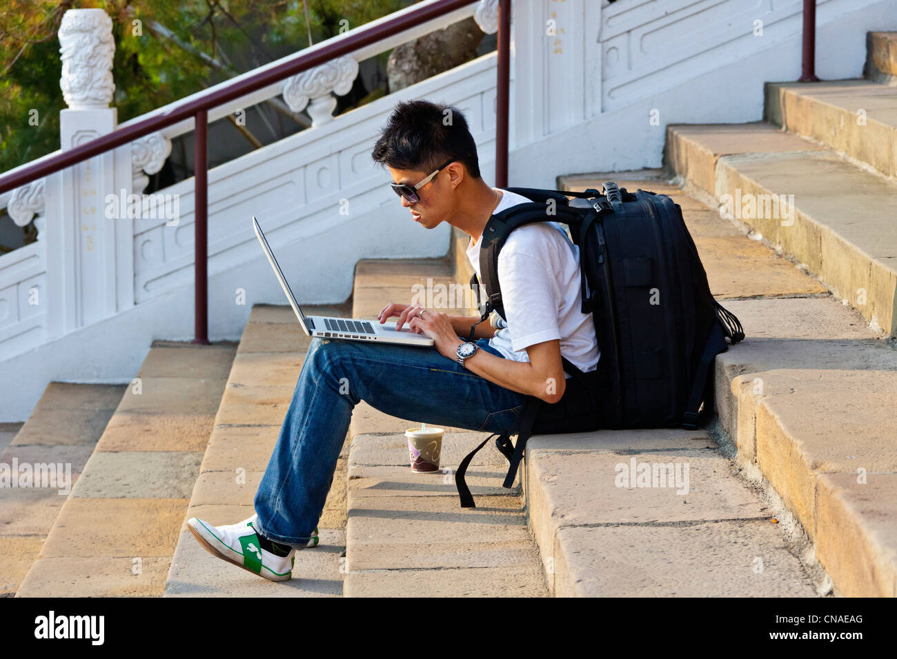 Young man working on Apple MacBook laptop computer seated on the steps ...