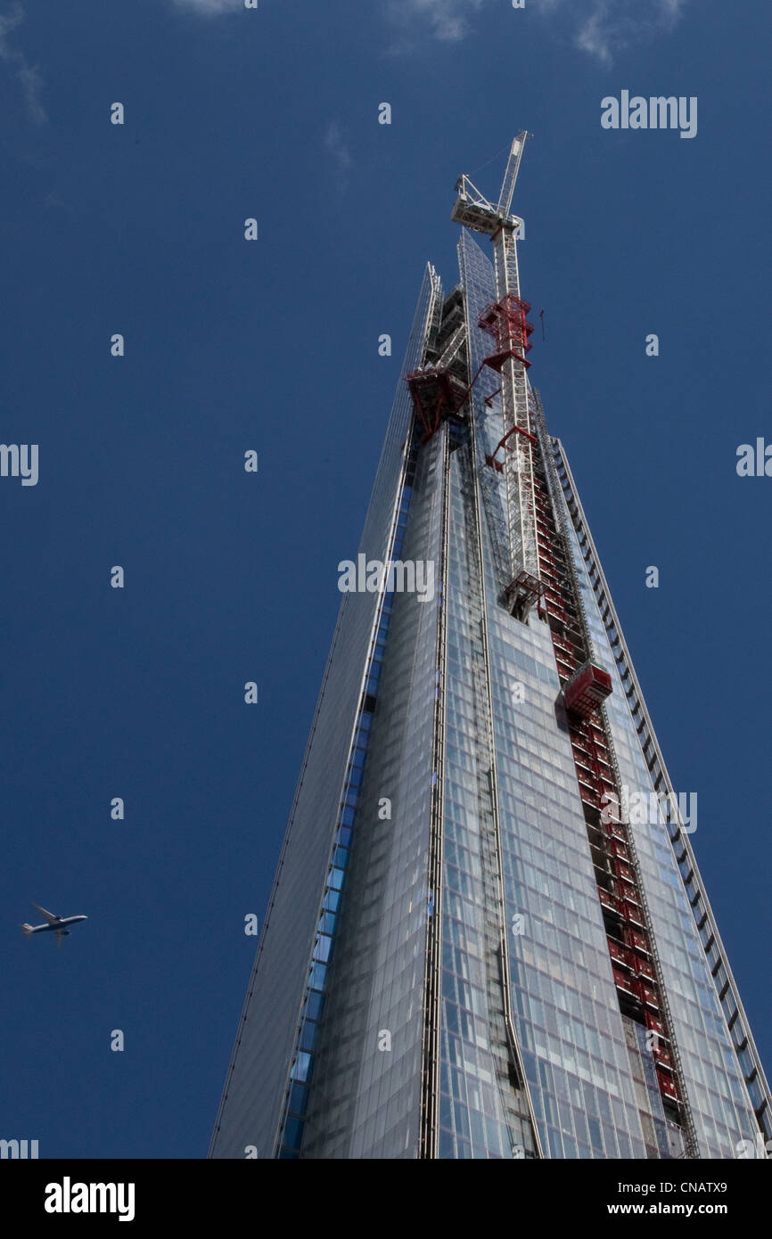 Spire of the London Shard against blue sky with passing jet airliner ...
