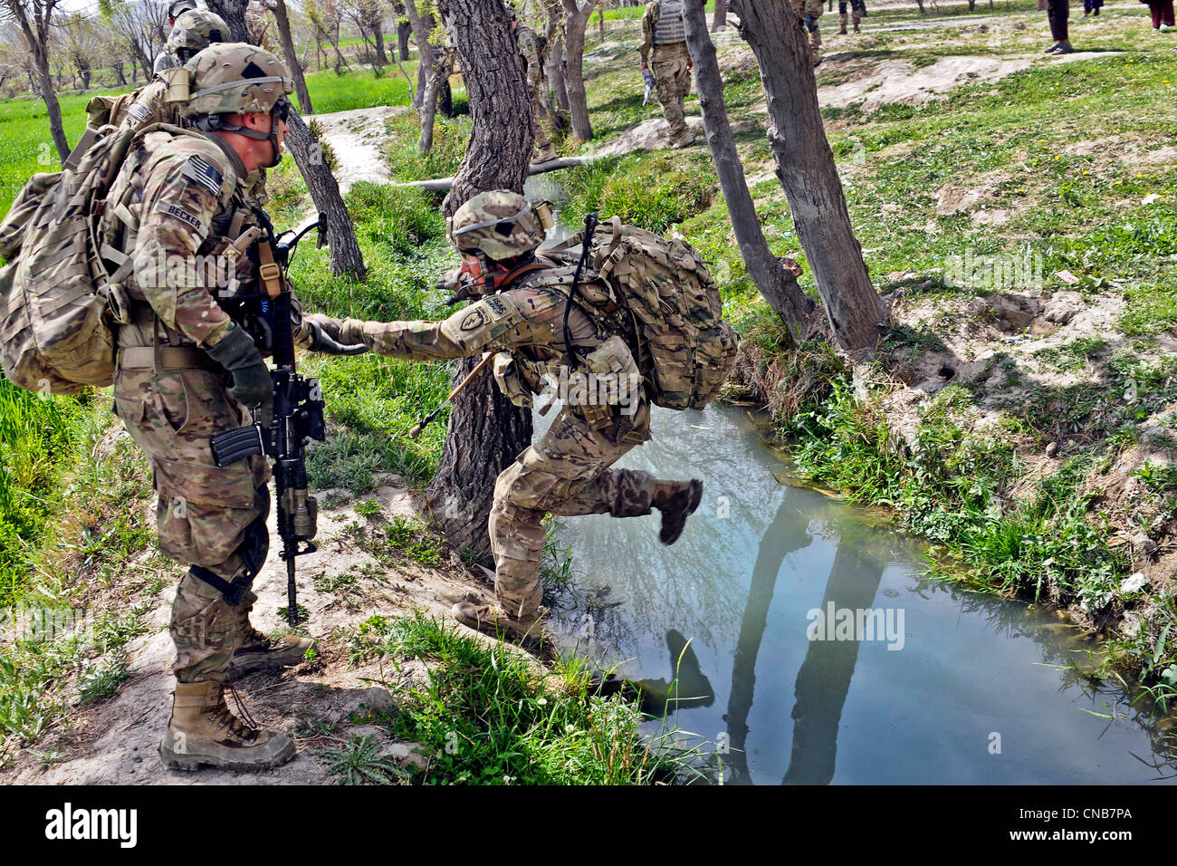 A US Army soldier leaps over an irrigation canal helped by a fellow ...