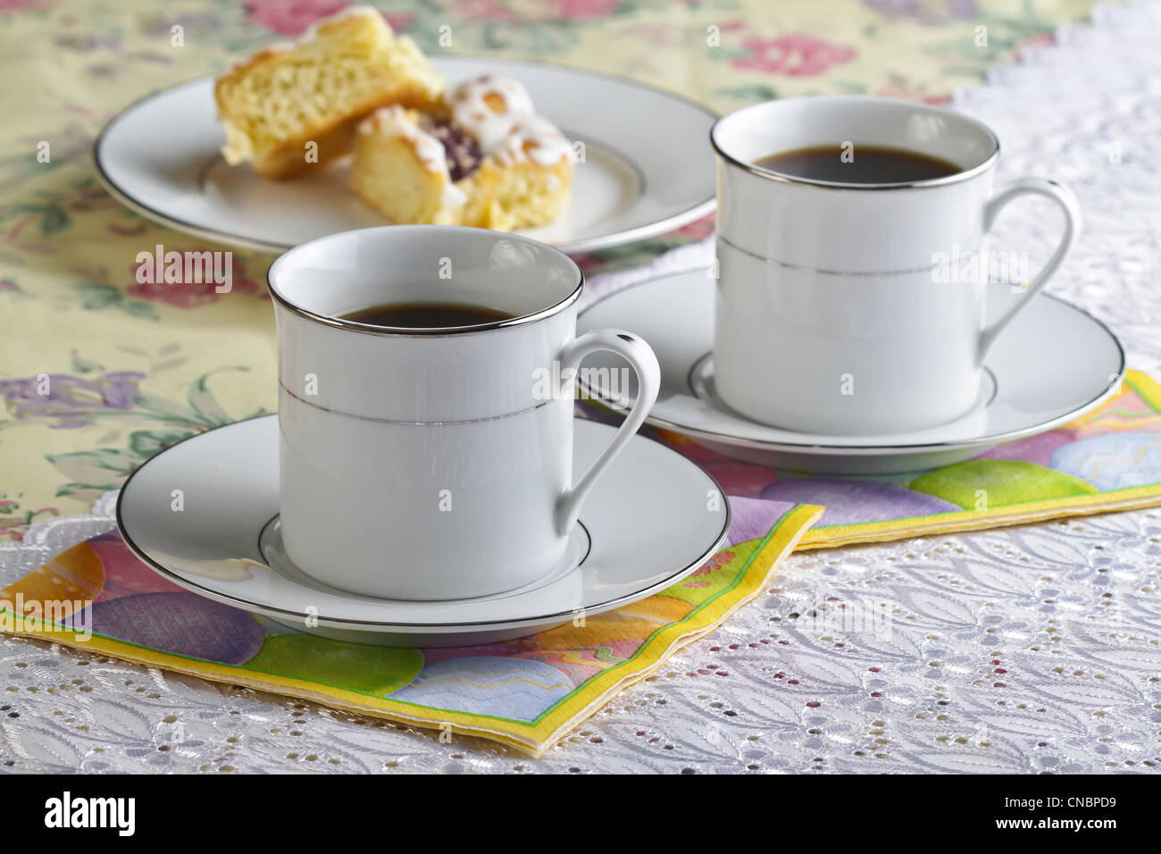 A table setting of china dishes with 2 cups of black coffee with ...