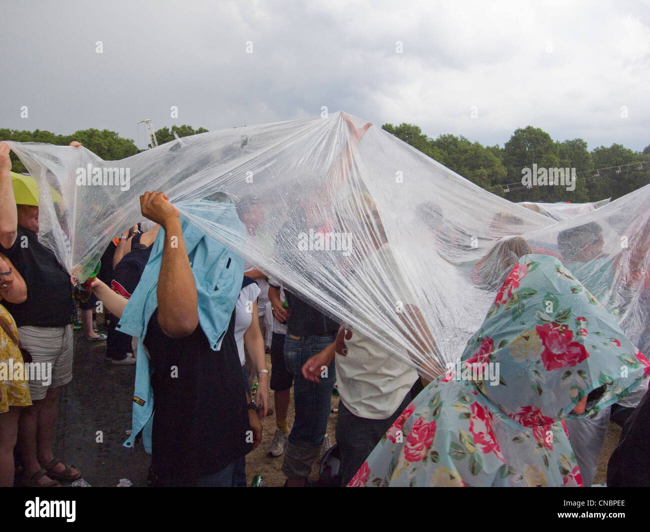 A crowd sheltering from the rain under a sheet of plastic at an outdoor ...