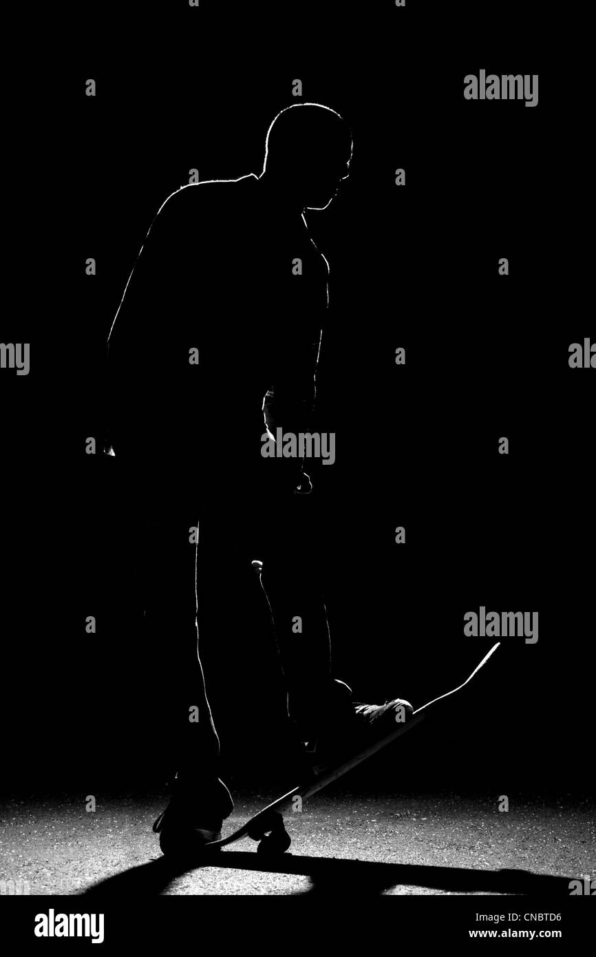 A backlit skateboarder guy posing under dramatic rim lighting with his ...