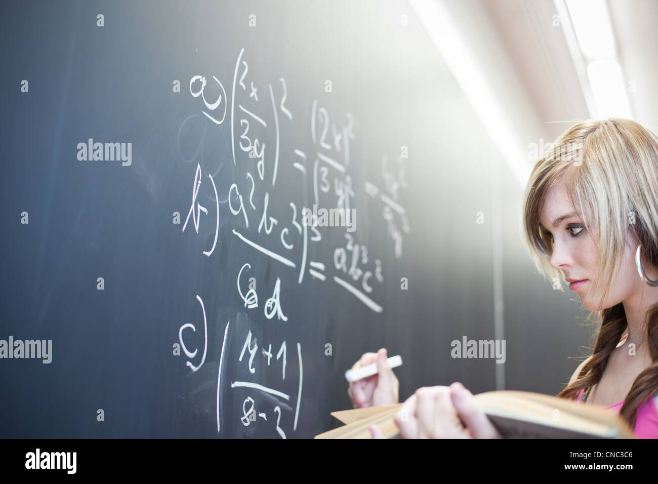 pretty young college student writing on the chalkboard/blackboard ...