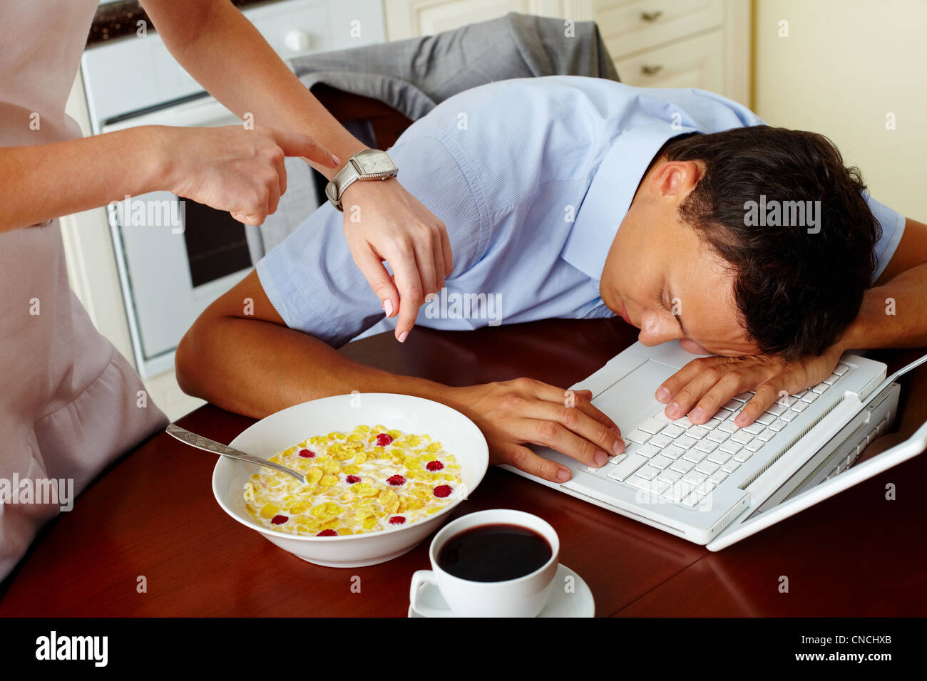 Portrait of man sleeping on laptop keypad with bowl of snacks and cup ...