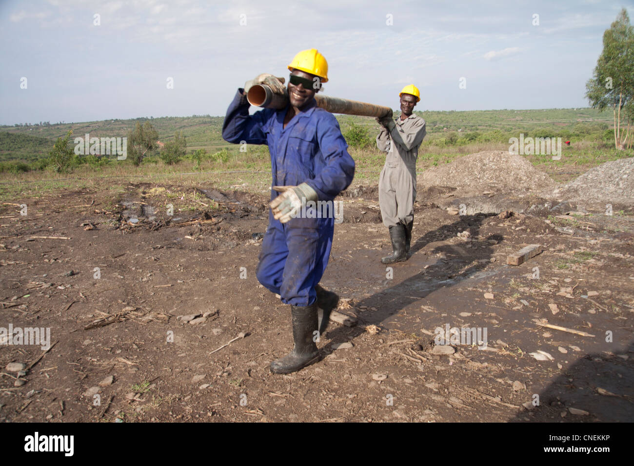 Two male drill rig assistants carry a drill rod to the drill rig in ...