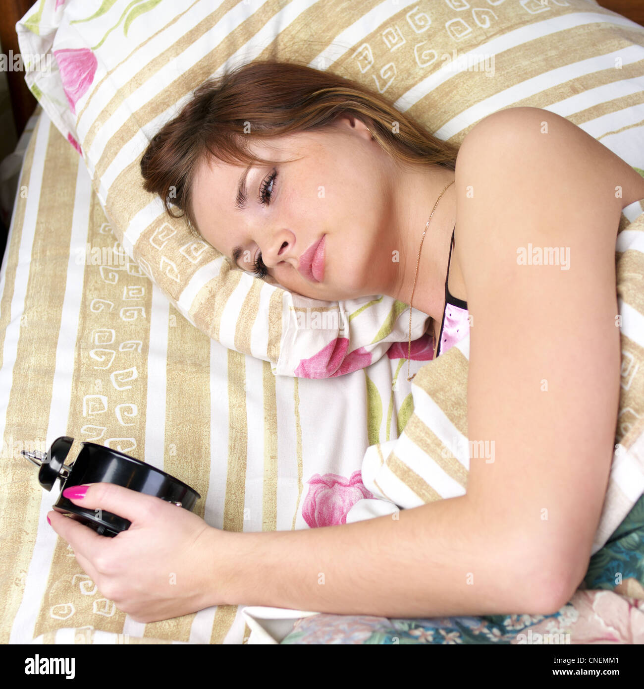 Drowsy girl in the bed looking to alarm clock Stock Photo - Alamy
