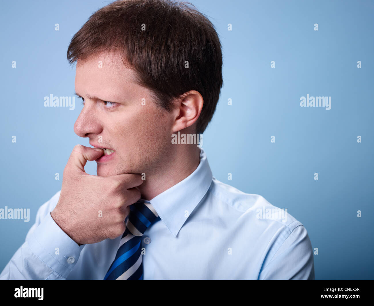 stressed mid adult businessman biting fingernails against blue ...