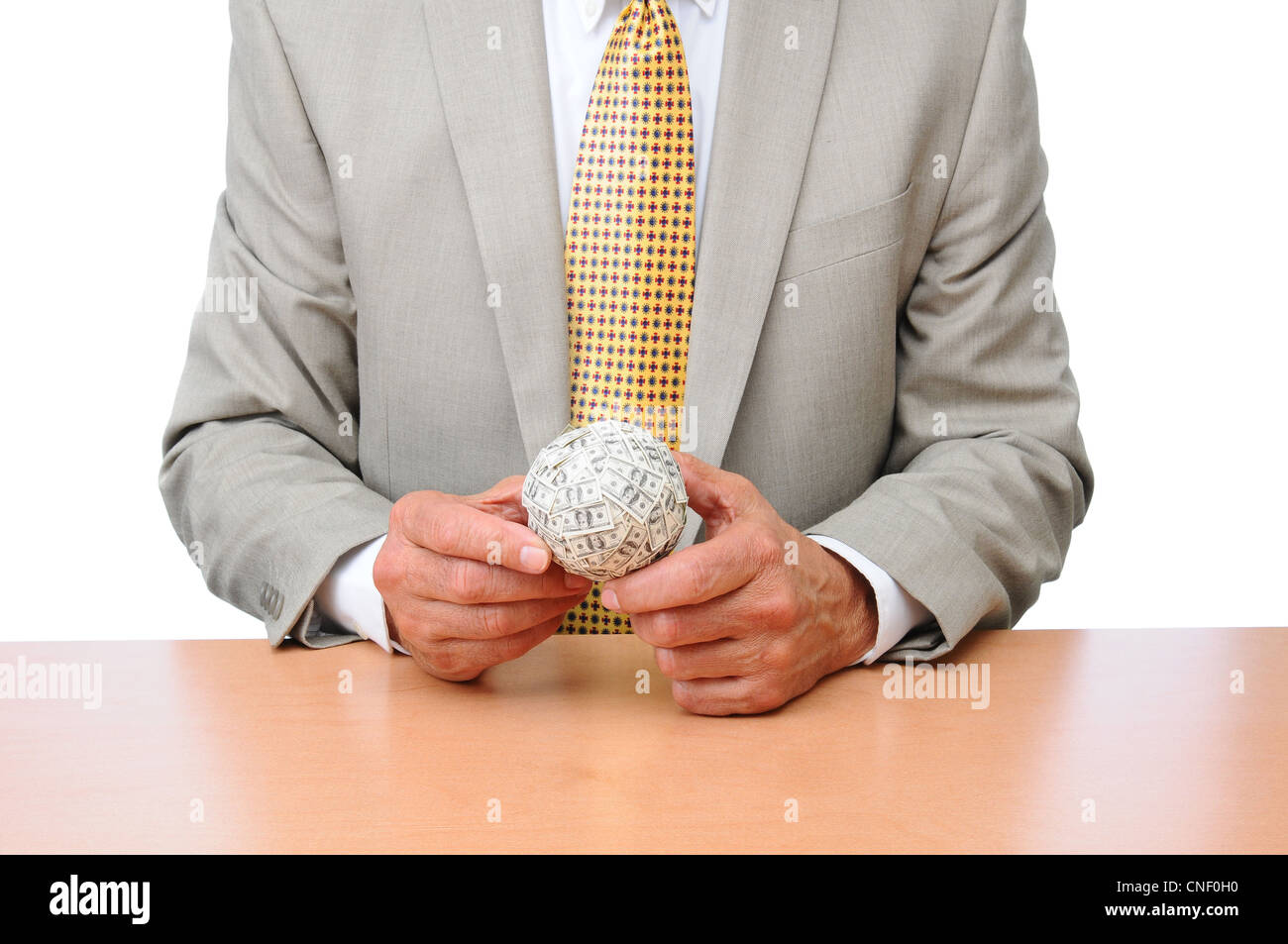 Closeup of a businessman seated at his desk holding a ball of money in ...
