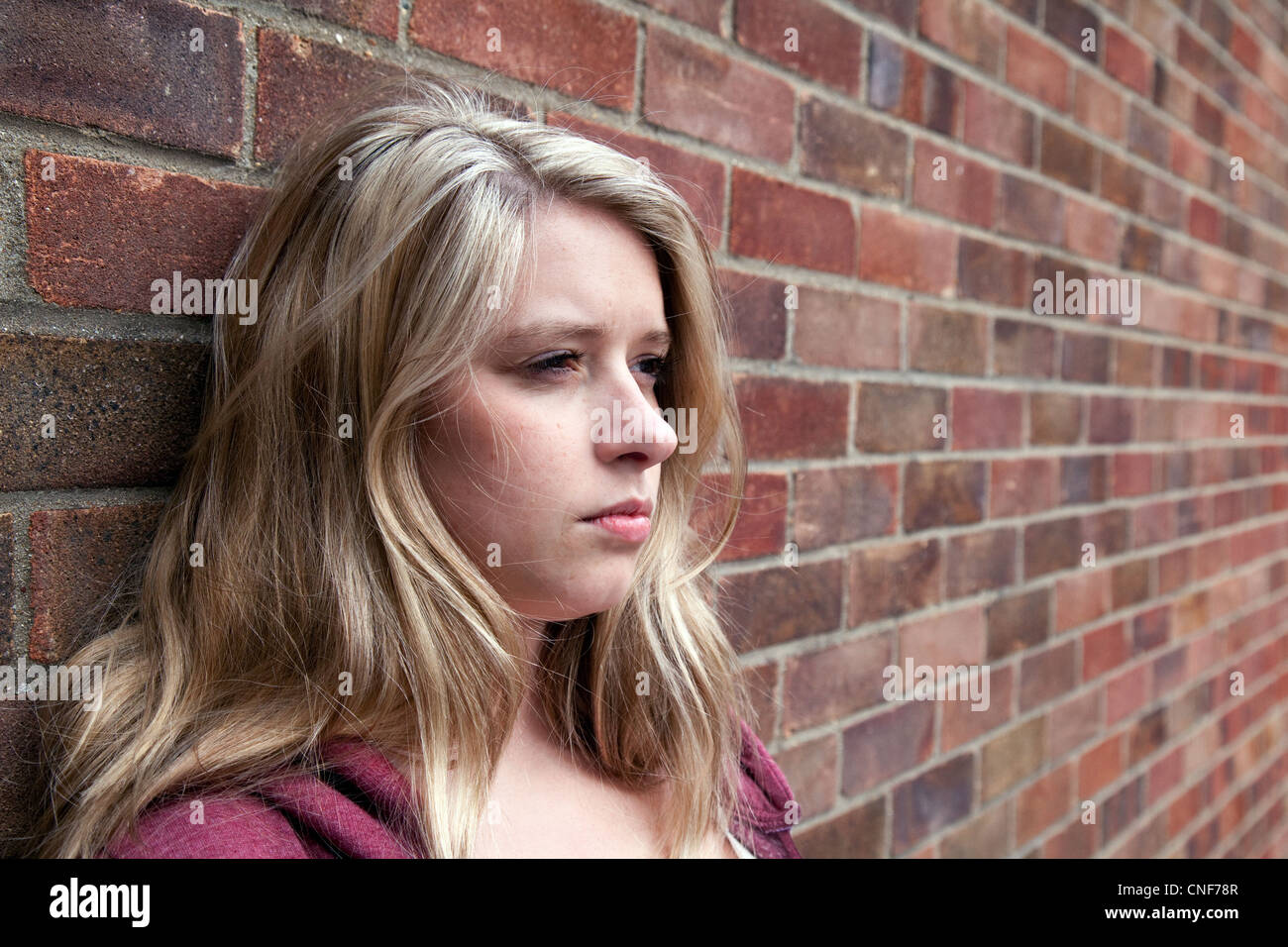 Blonde teenage girl leaning on a brick wall, head and shoulders ...