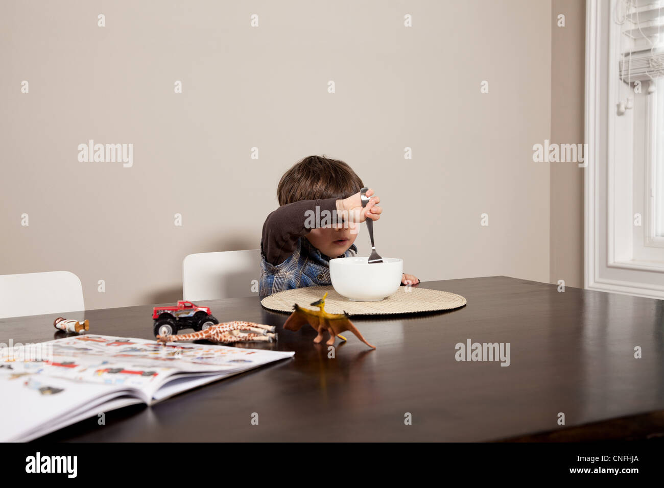 Boy at table with bowl of food and toys Stock Photo - Alamy