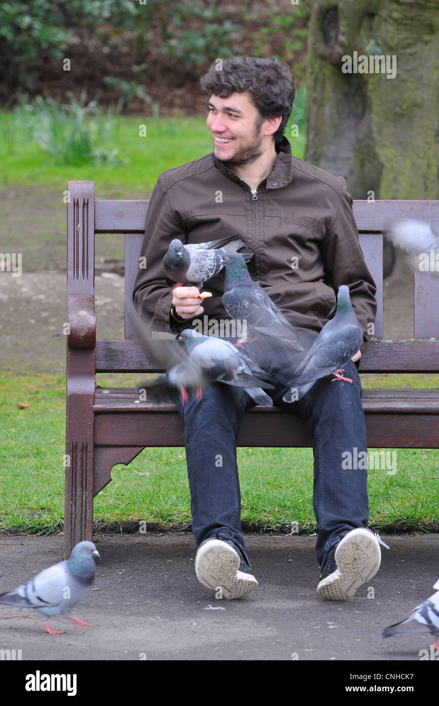 Young Scottish man sitting on a bench, feeding birds ( pigeons ) and ...