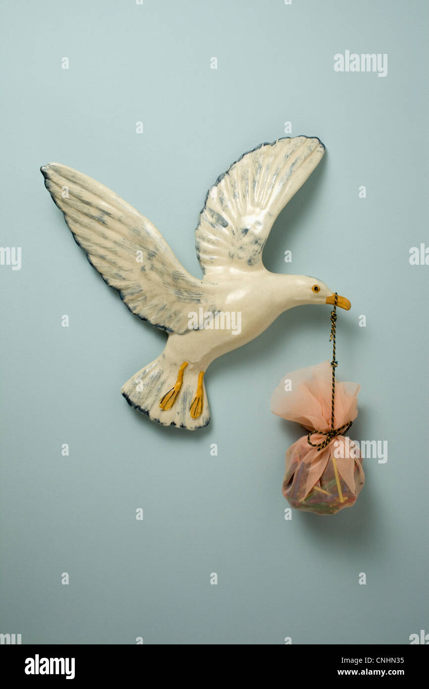 A plastic bird carrying a sack in its beak, hanging on wall Stock Photo ...