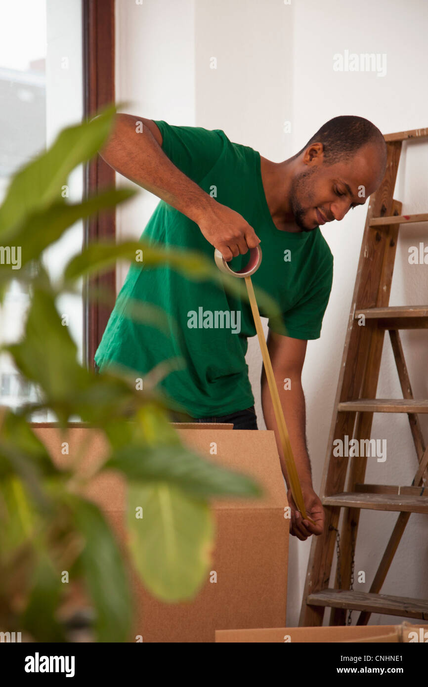 A man taping a moving box, focus on background Stock Photo - Alamy
