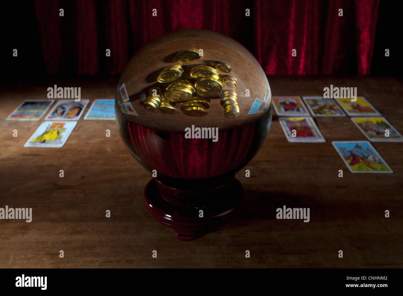 A crystal ball with gold coins in the reflection and tarot cards in ...