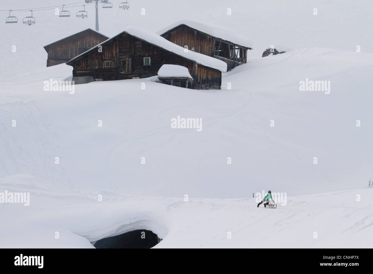 Child on sledge below log cabins on snowy hill Stock Photo - Alamy