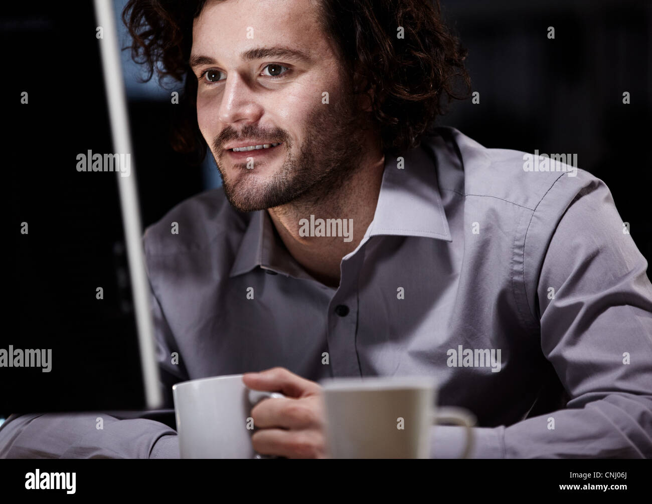 Young man looking at computer monitor, working late Stock Photo - Alamy