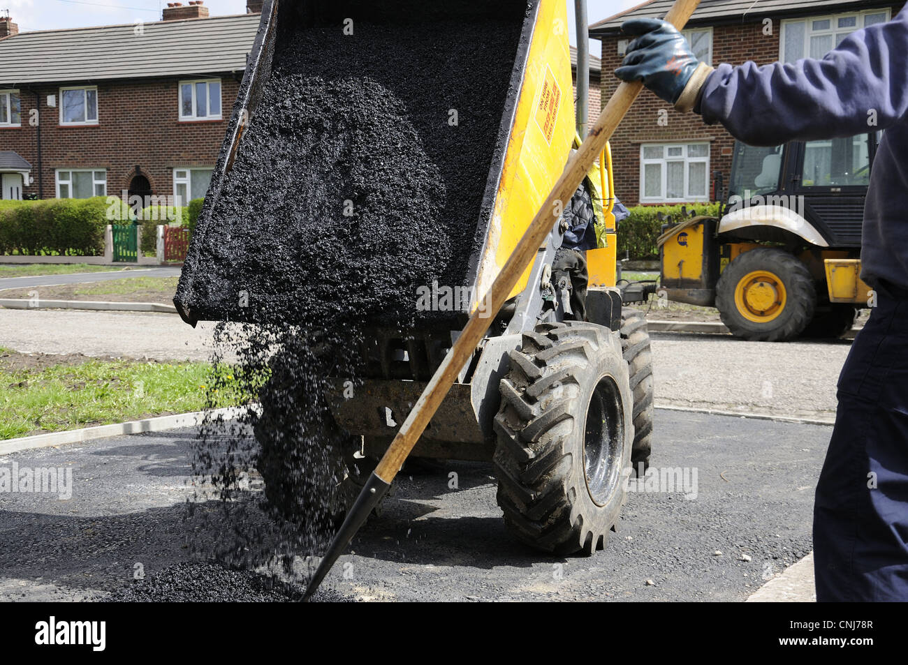 Small yellow tipper truck dropping asphalt to be spread and raked Stock ...