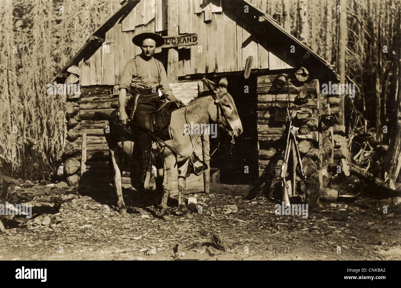 Heavily Armed Cowboy Riding Donkey at Log Cabin Stock Photo - Alamy