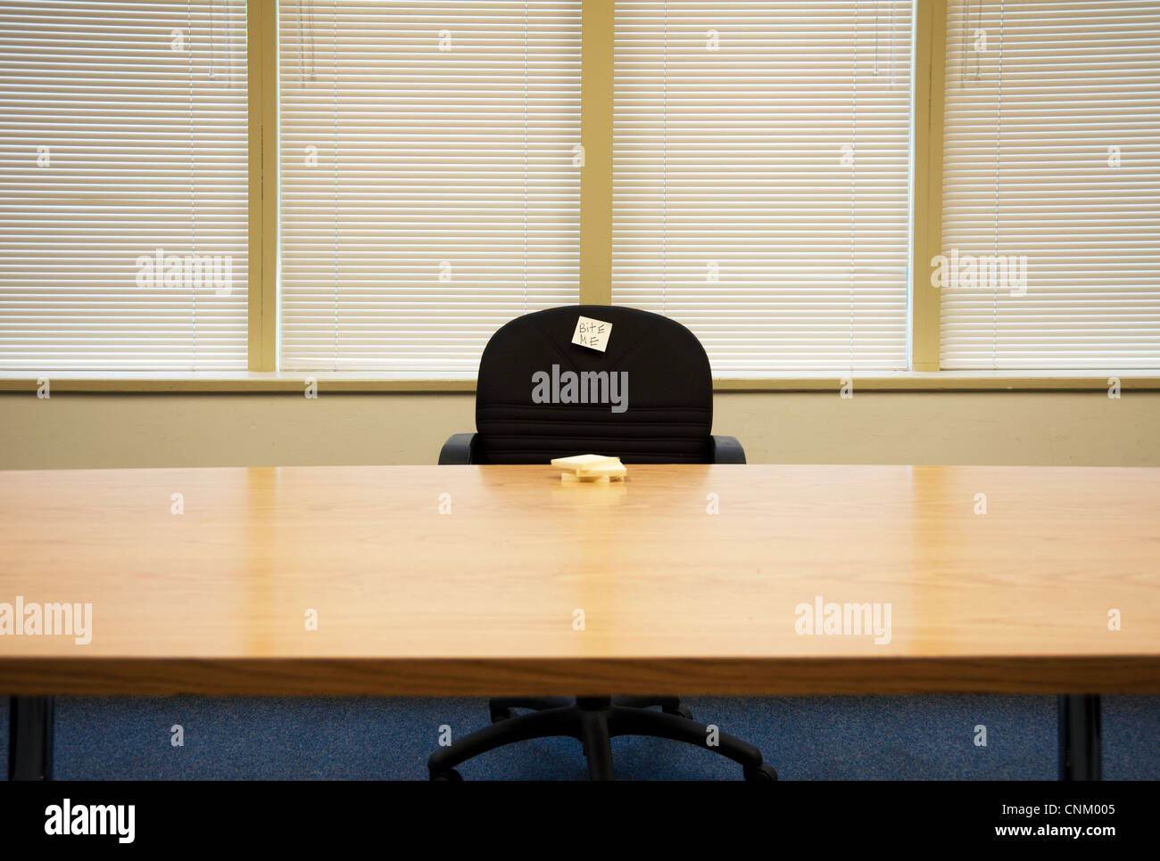 Empty chair at boardroom table with sticky note that says "bite me ...