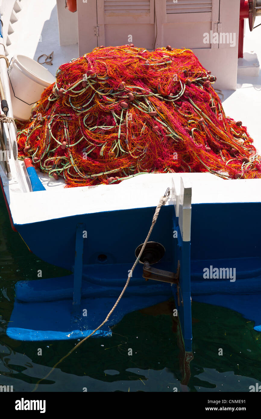 Brightly coloured fishing nets piled on a small traditional fishing ...