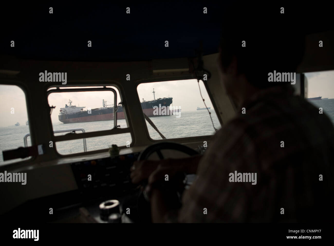 A boat driver navigates past one of the several hundred ships at anchor ...