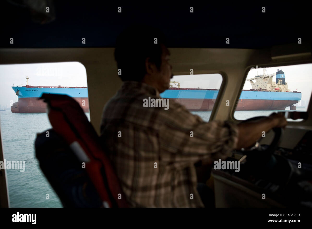 A boat driver navigates past one of the several hundred ships at anchor ...