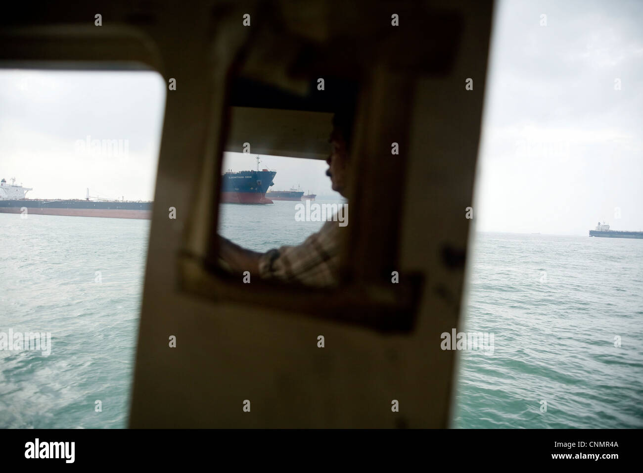 A boat driver navigates past one of the several hundred ships at anchor ...