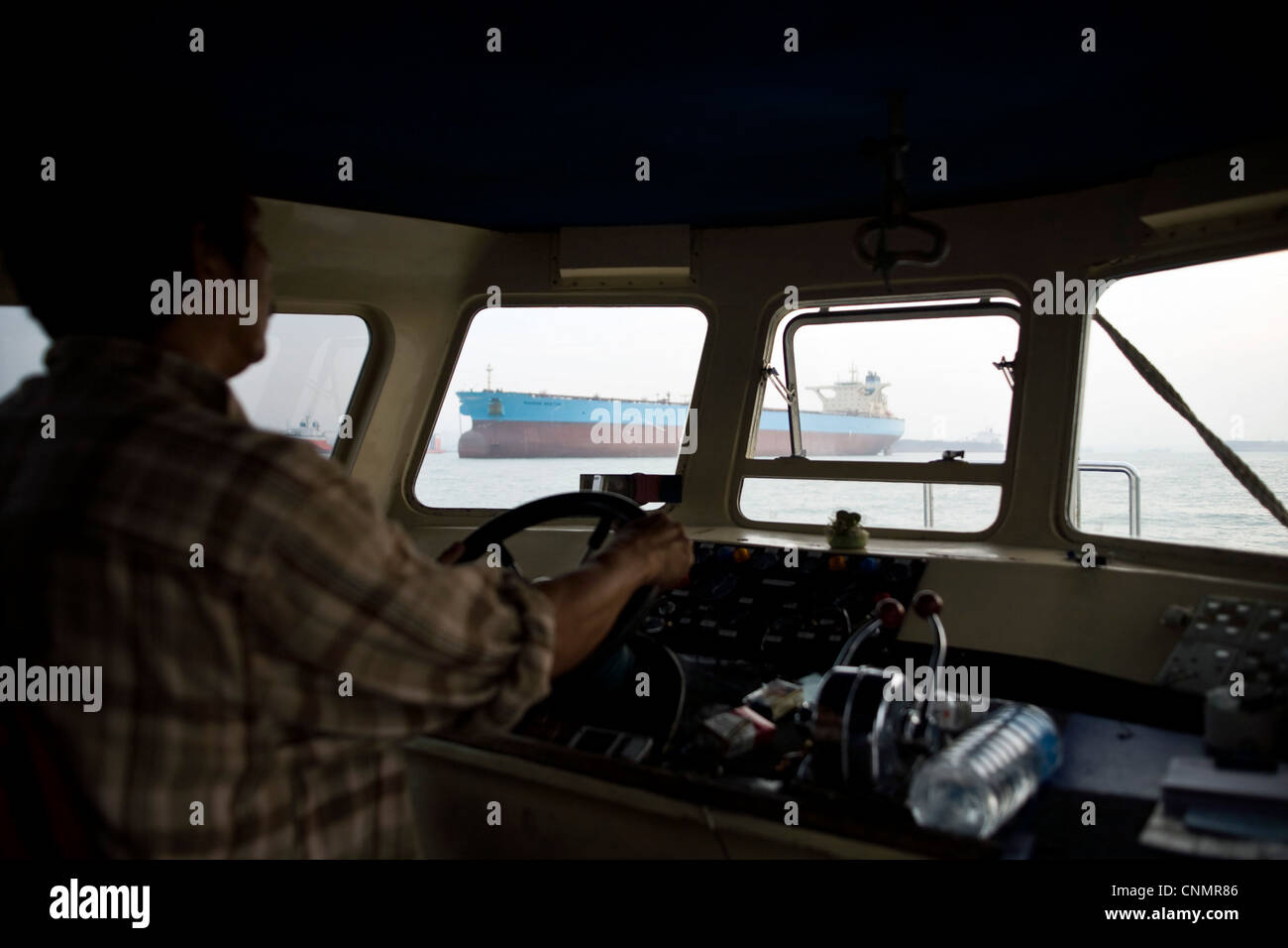 A boat driver navigates past one of the several hundred ships at anchor ...