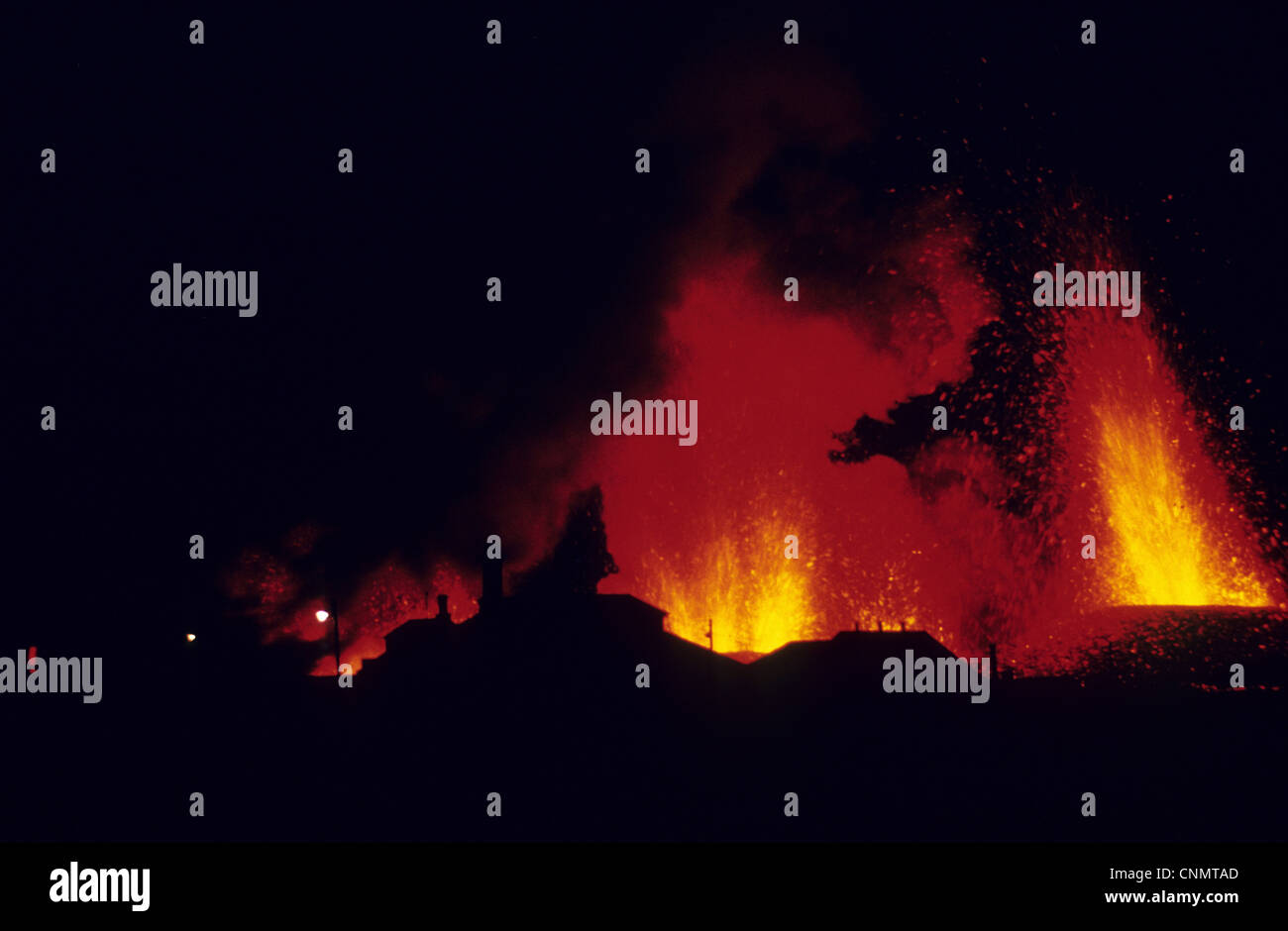 Volcanic eruption, with erupting lava and town buildings silhouetted ...