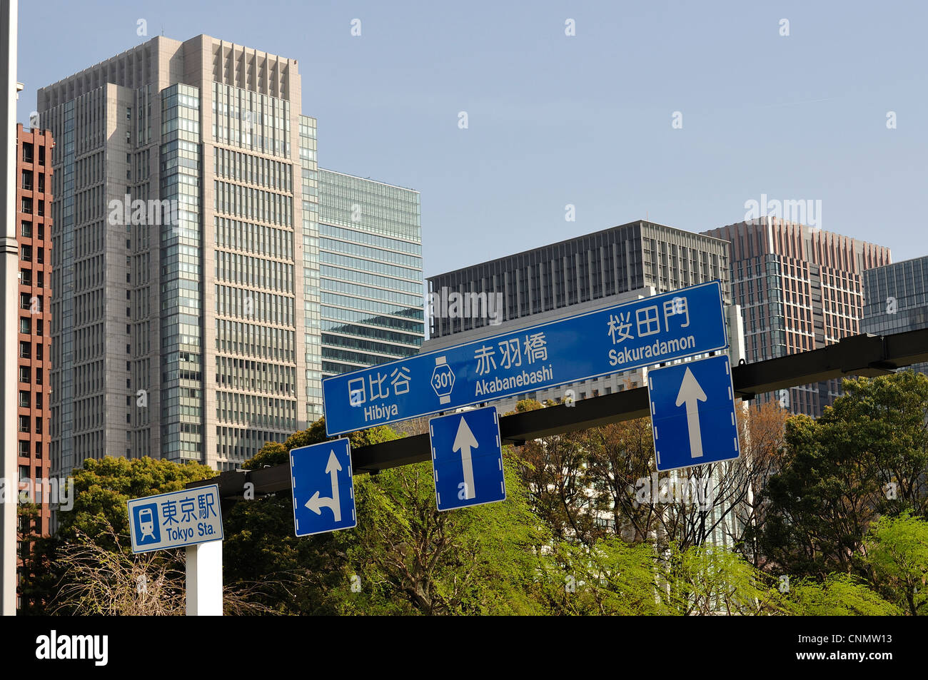 Blue/white road signs over major road with skyscrapers in background ...