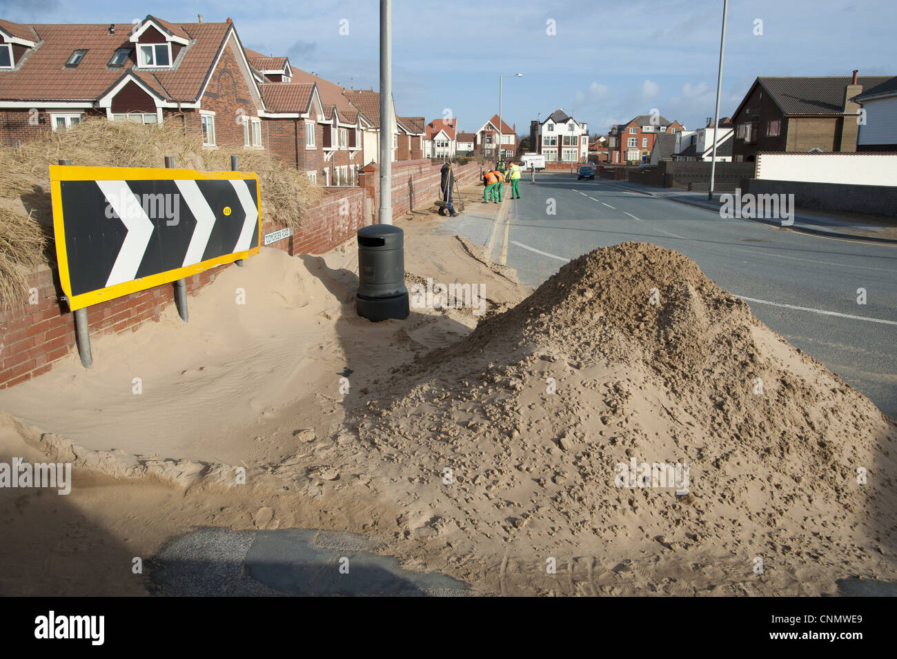 Council workers clearing away sand blown beach dunes onto road pavement ...