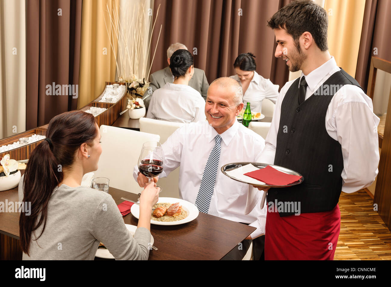 Business lunch executive people toast with red wine young waiter serve ...