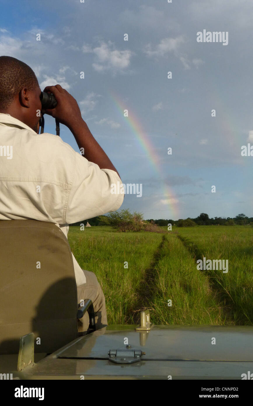 'Spotter' sitting at front of safari vehicle, in wetland habitat with ...