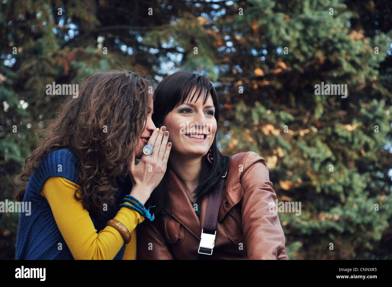 Young women whispering in friend's ear outdoors Stock Photo - Alamy