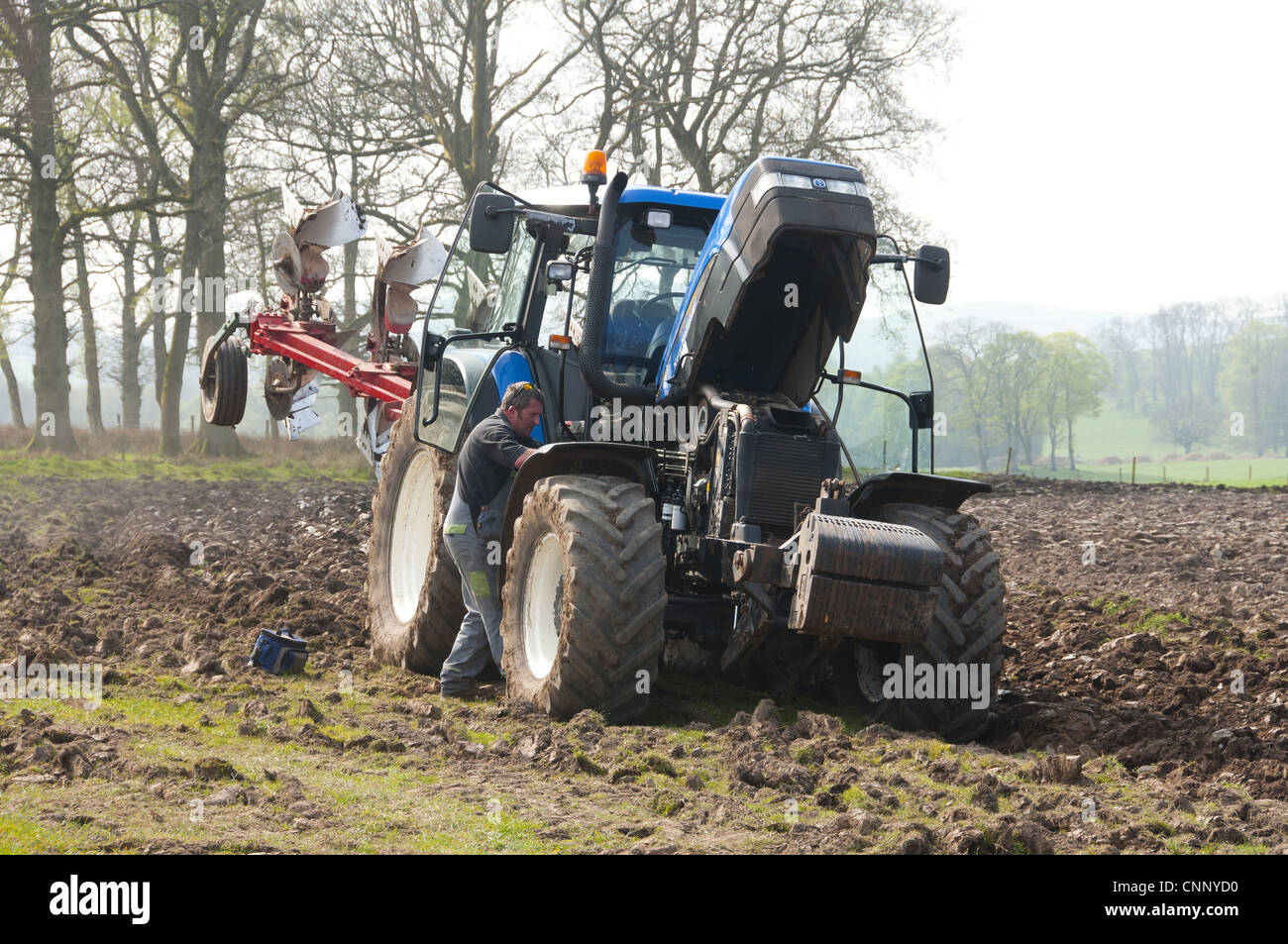 Farmer repairing New Holland tractor with plough in field, Lochmaben ...