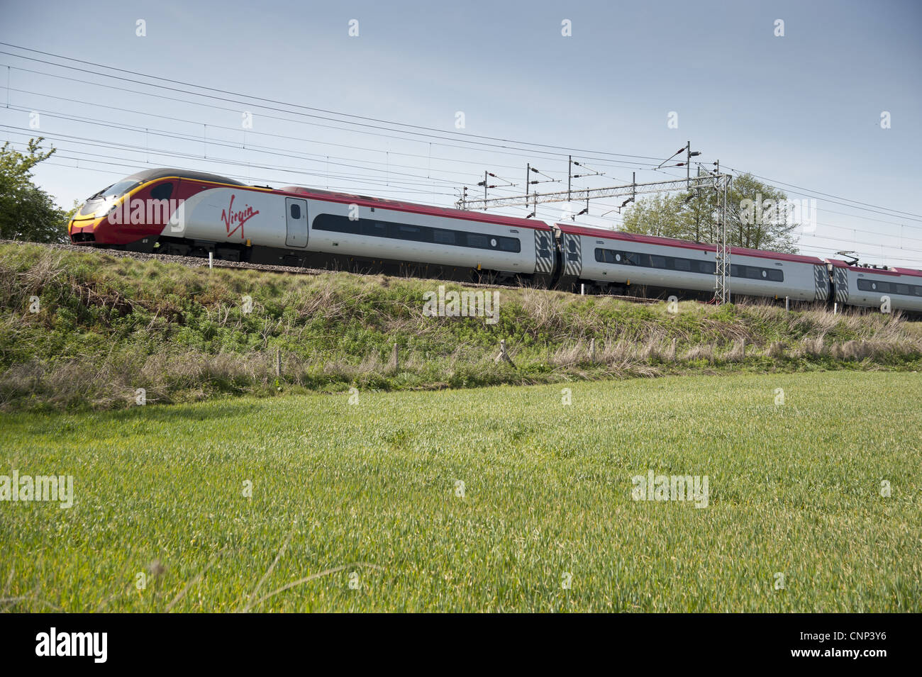 Virgin railway train travelling along bank in farmland, Wrinehill ...